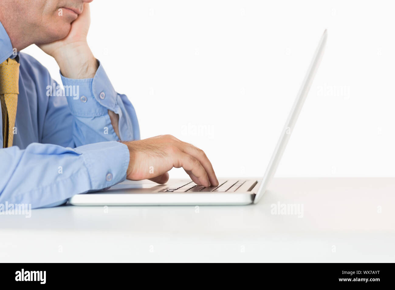 Well-dressed man writing on his laptop on his desk in a white ...