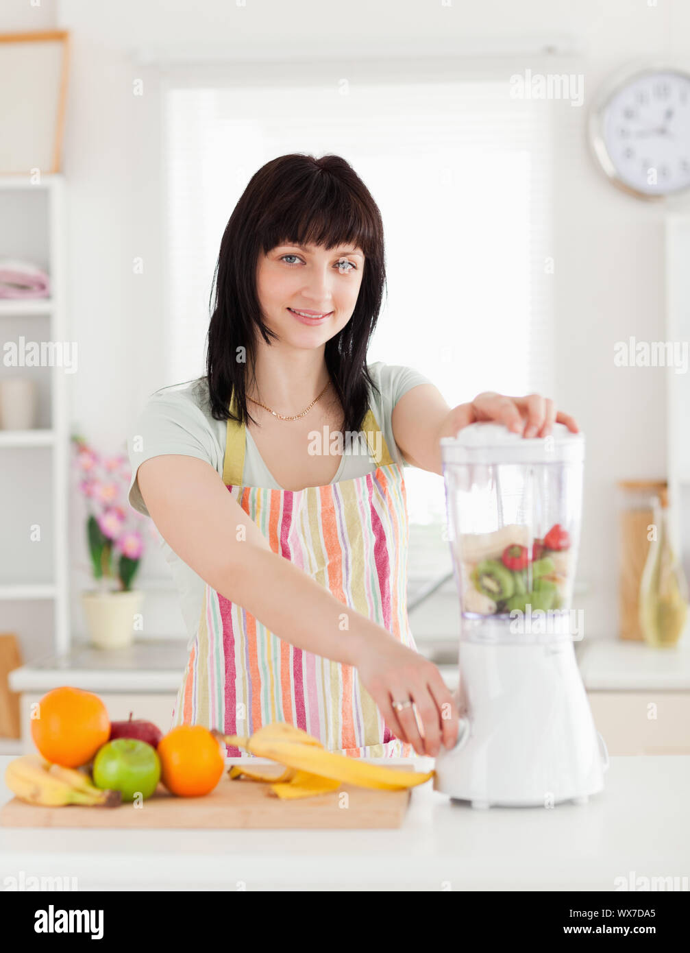 Beautiful brunette woman using a mixer while standing in the kitchen ...