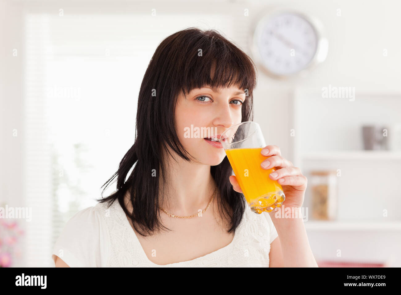 Pretty brunette drinking a glass of orange juice while standing in the ...