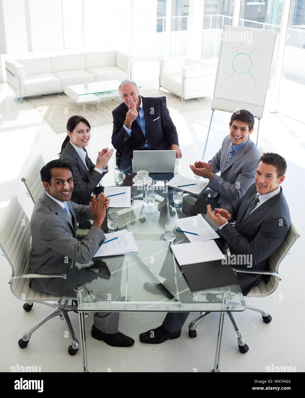 International business team clapping sitting around a conference table ...