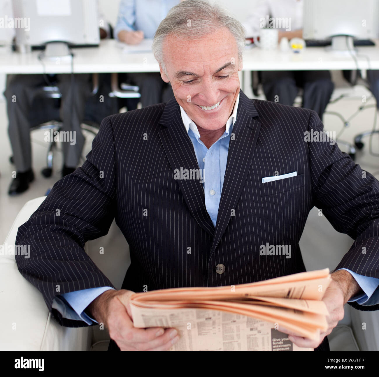 Senior businessman reading a newspaper with his team in the background ...