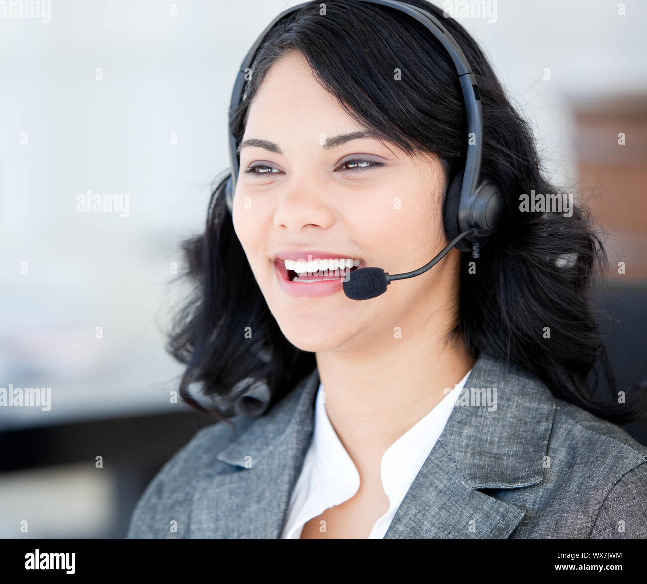 Joyful businesswoman wearing a headset to talk with customer in the ...