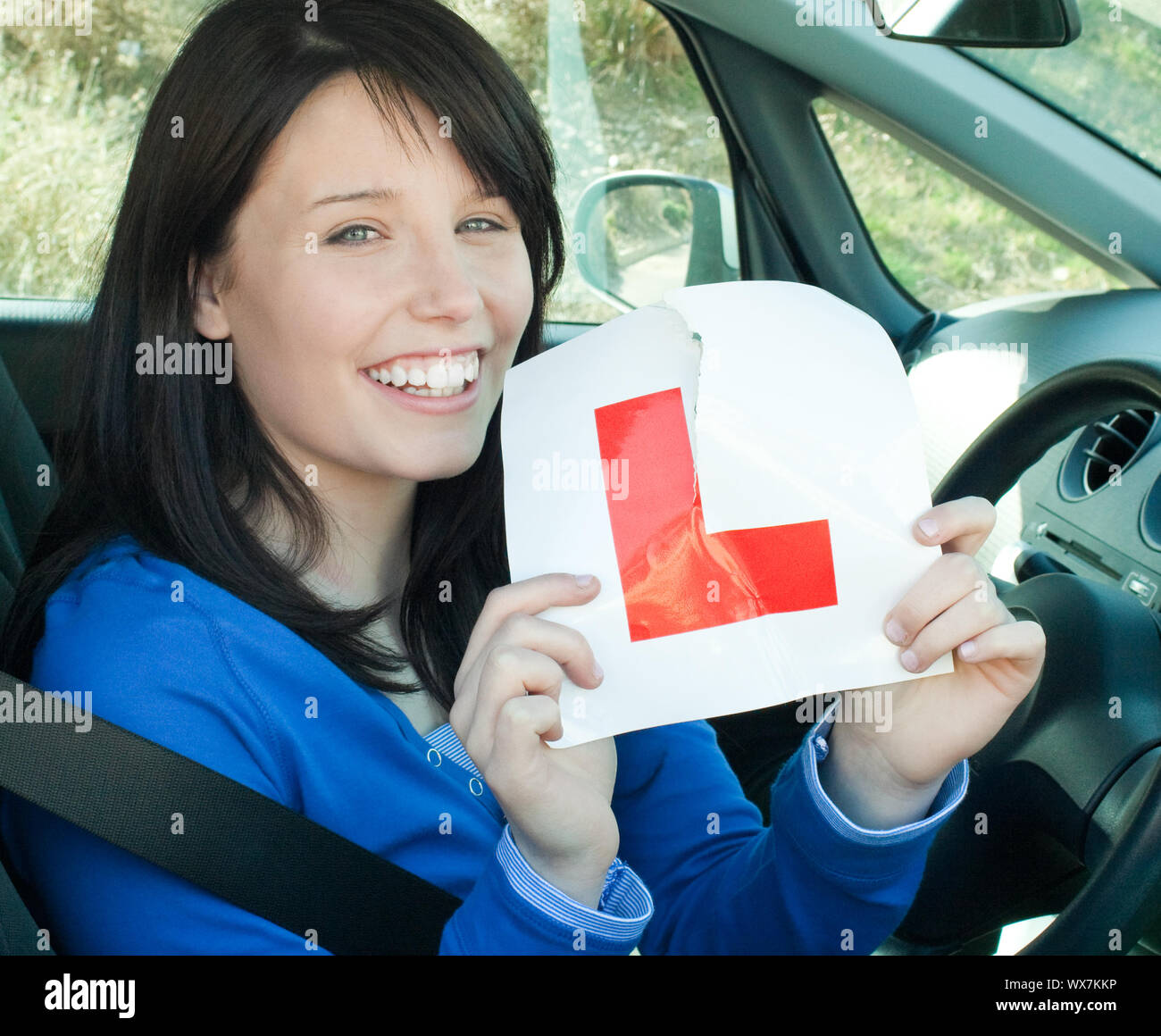 Happy teen girl sitting in her car tearing a L-sign after having her ...