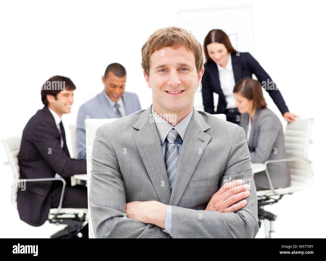 Assertive male executive with folded arms sitting in front of his team ...