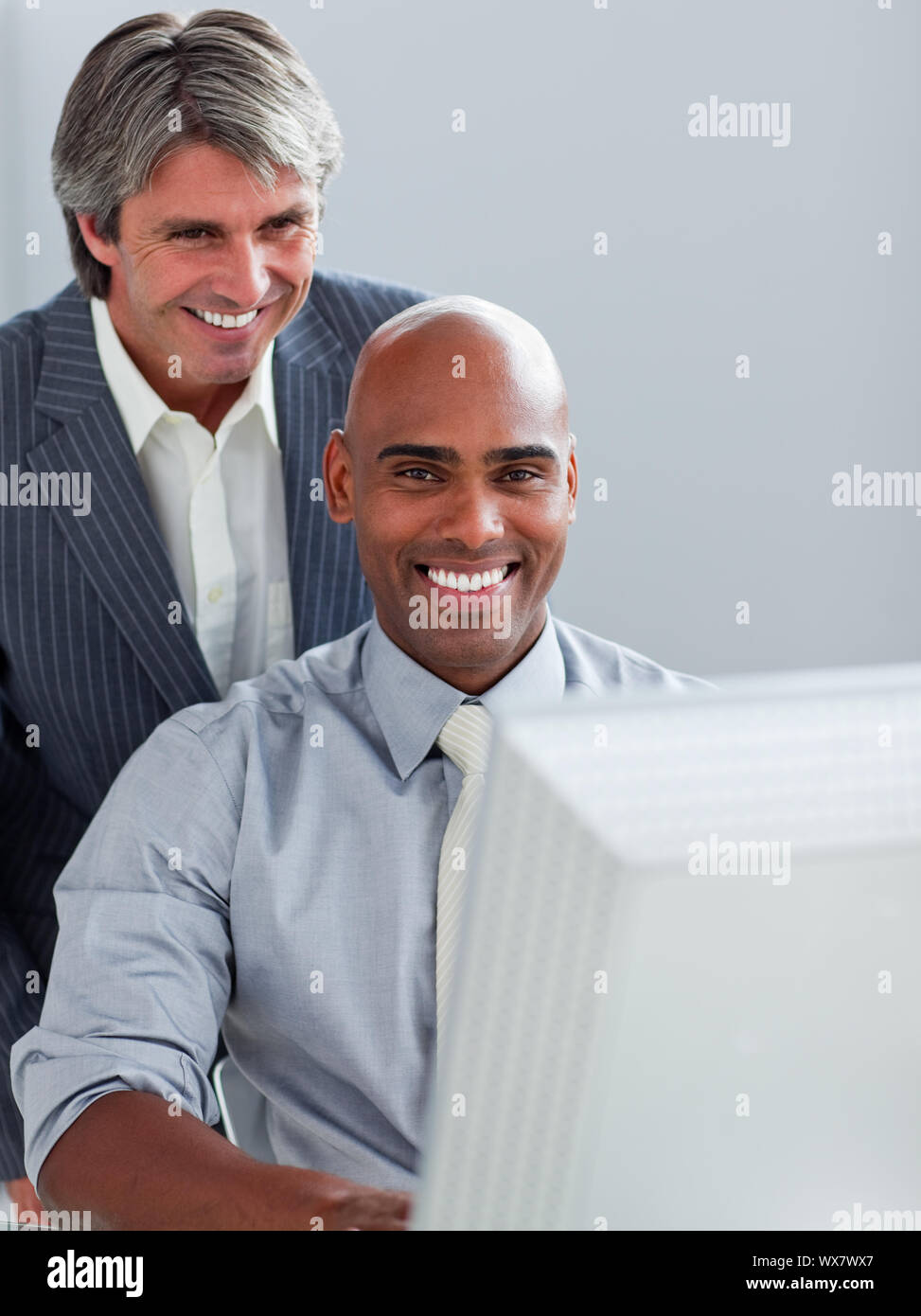 Mature businessman helping his colleague at a computer in the office ...