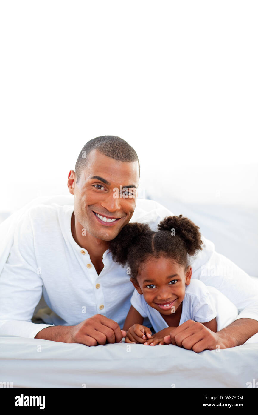 Attentive father and his daughter lying on a bed smiling at the camera ...