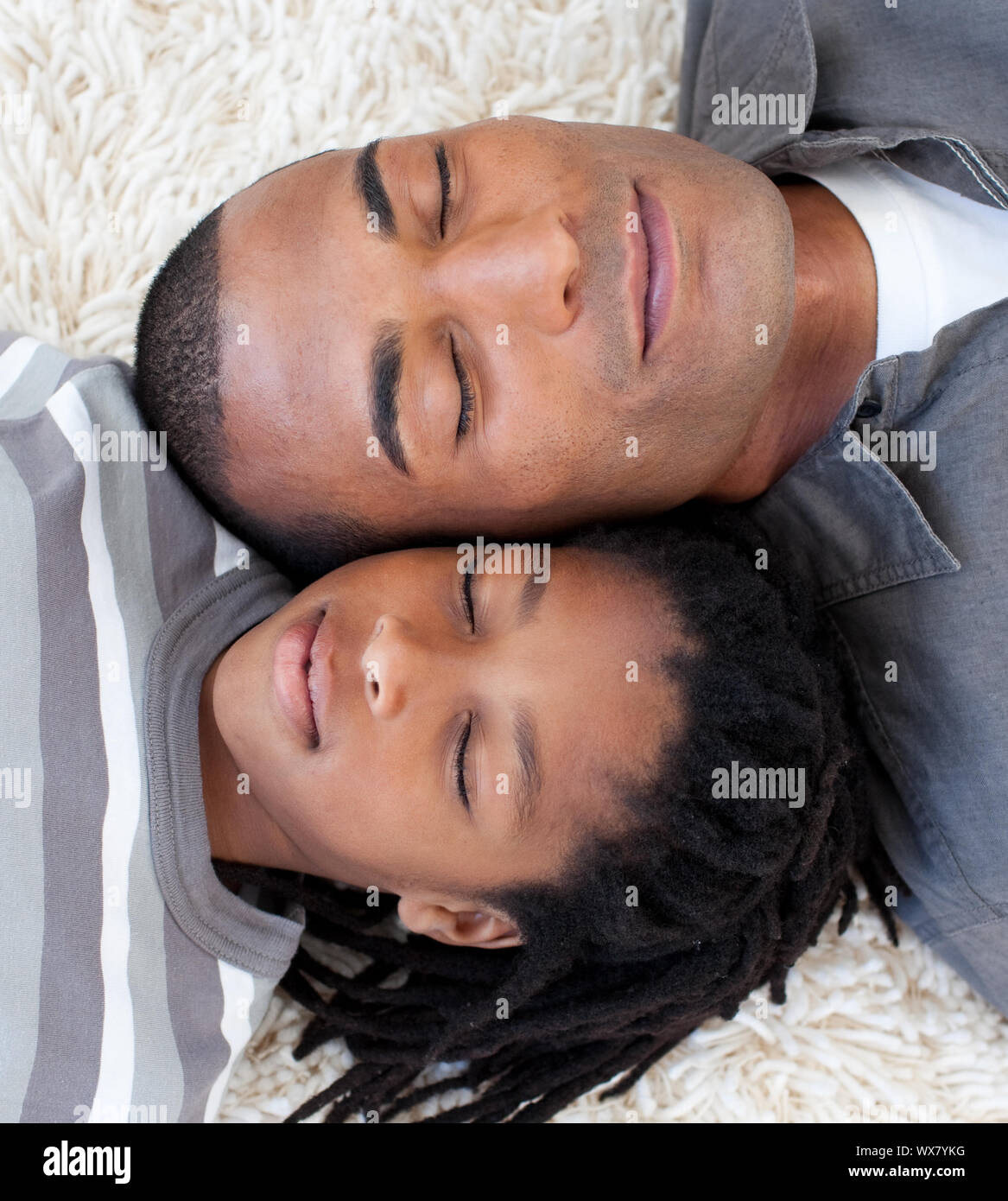 Portrait of Afro-American father and son sleeping on the floor at home ...