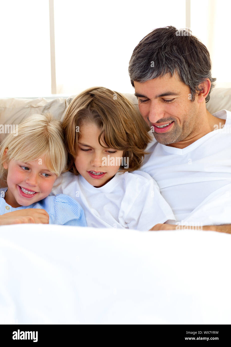 Attentive father and his children reading book lying in bed Stock Photo ...