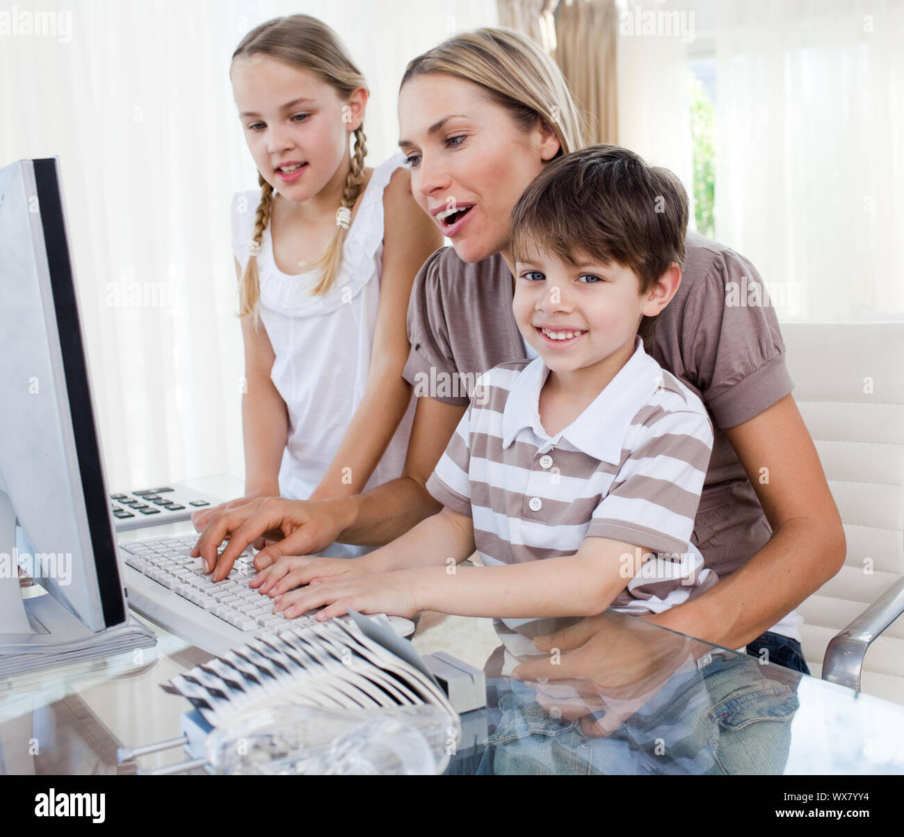 Smiling little boy at a computer with his mother and his sister Stock ...