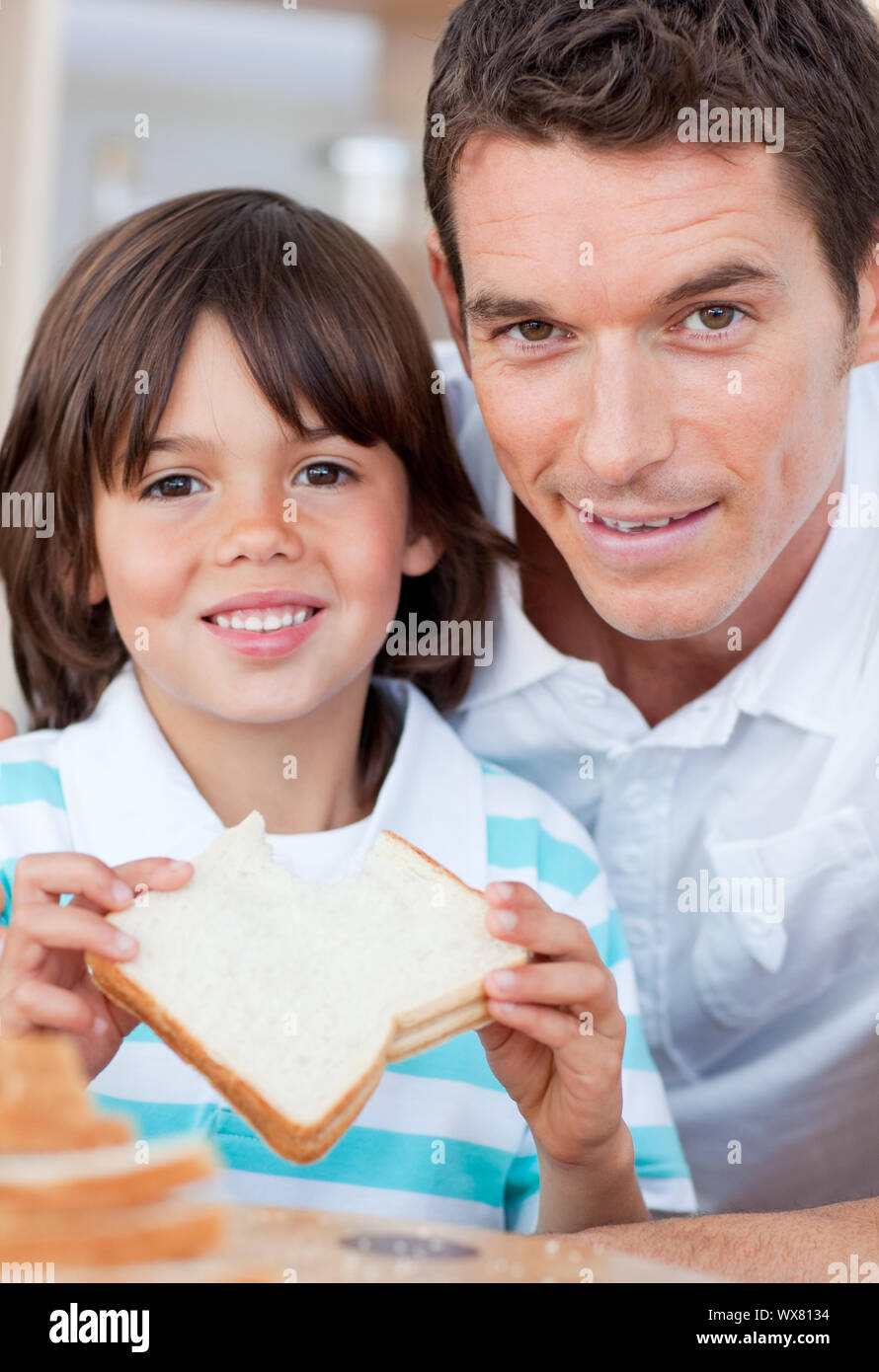 Portrait of a little boy and his father eating bread in the kitchen ...