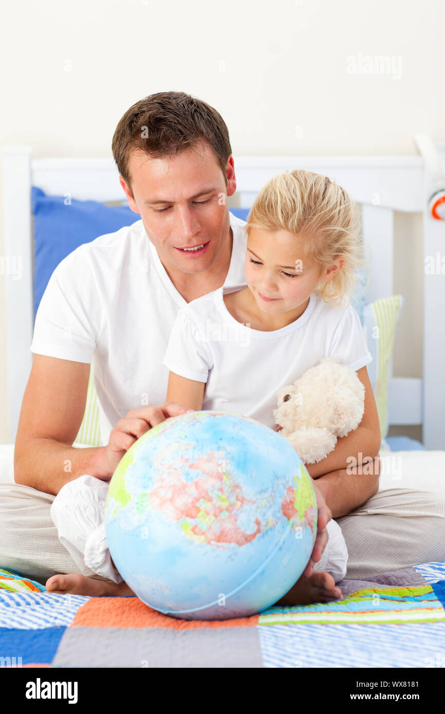 Attentive father and his daughter looking at a terretrial globe sitting ...