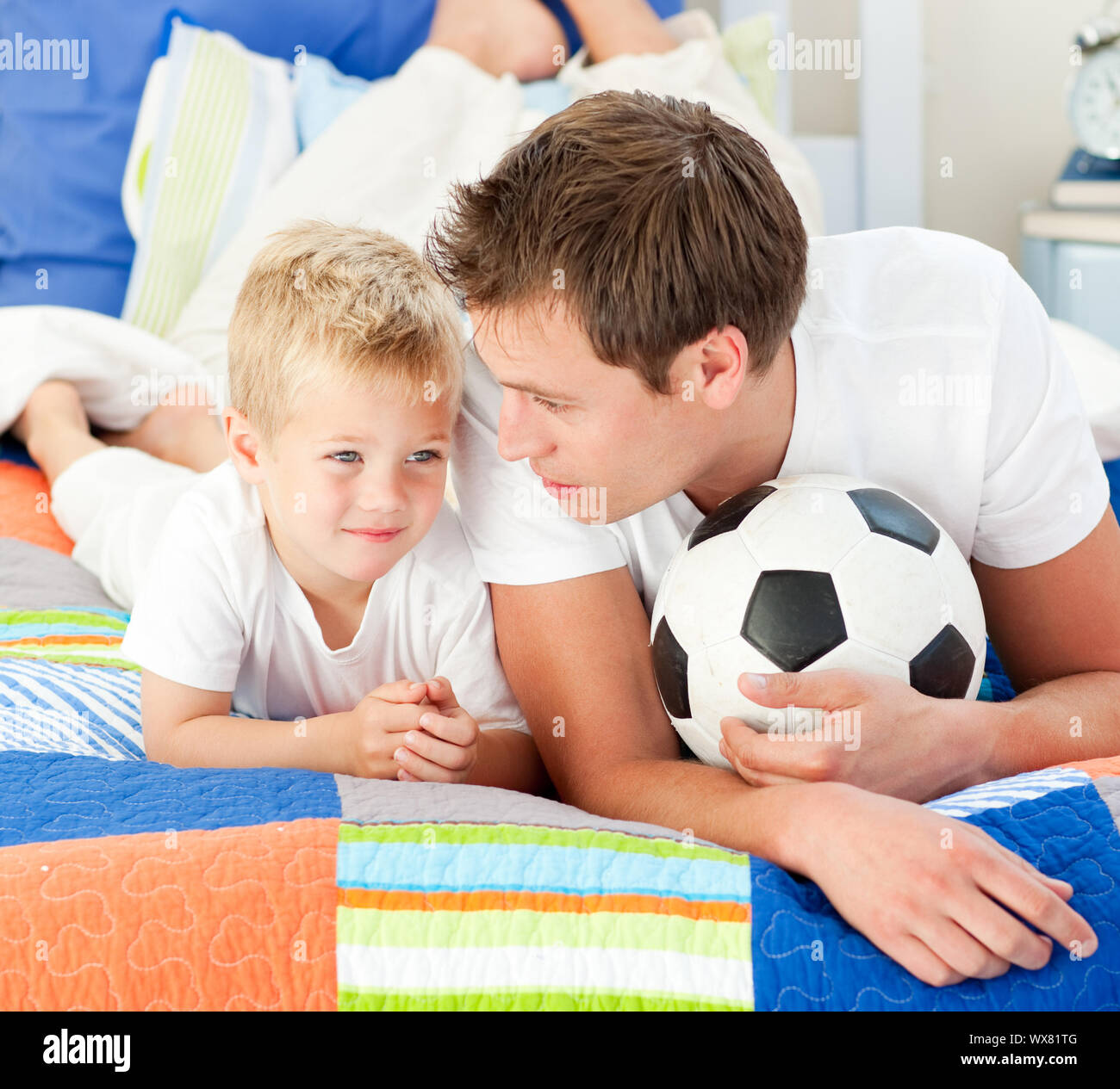 Attentive father and his son playing with a soccer ball lying on bed ...