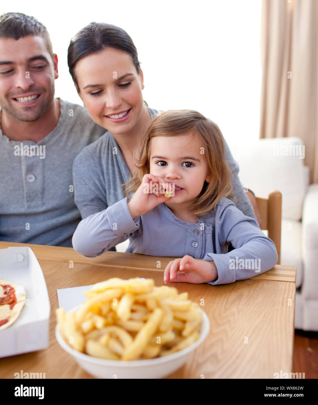 Little girl eating fries and pizza at home with her parents Stock Photo ...