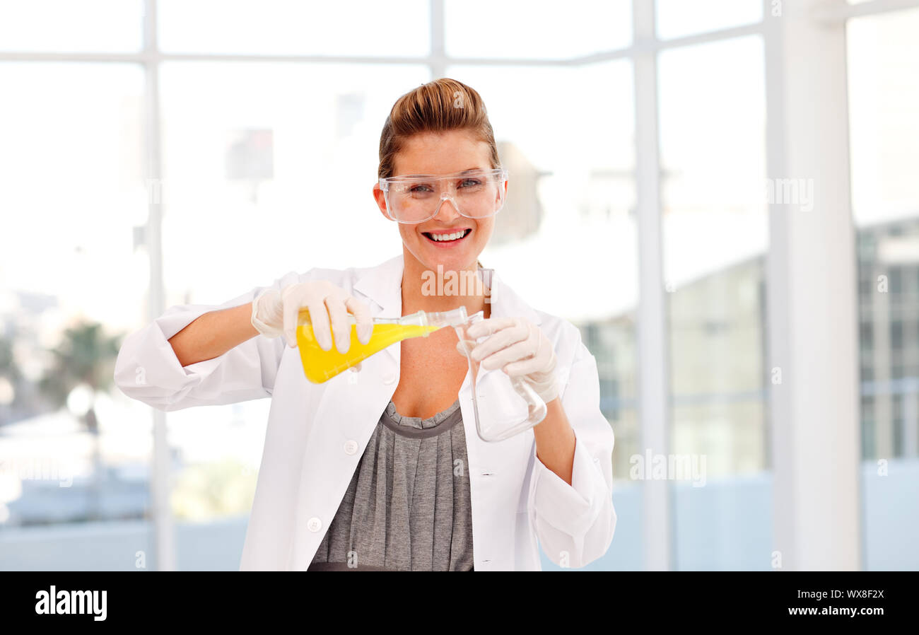 Attractive young scientist examining a test-tube smiling at the camera ...