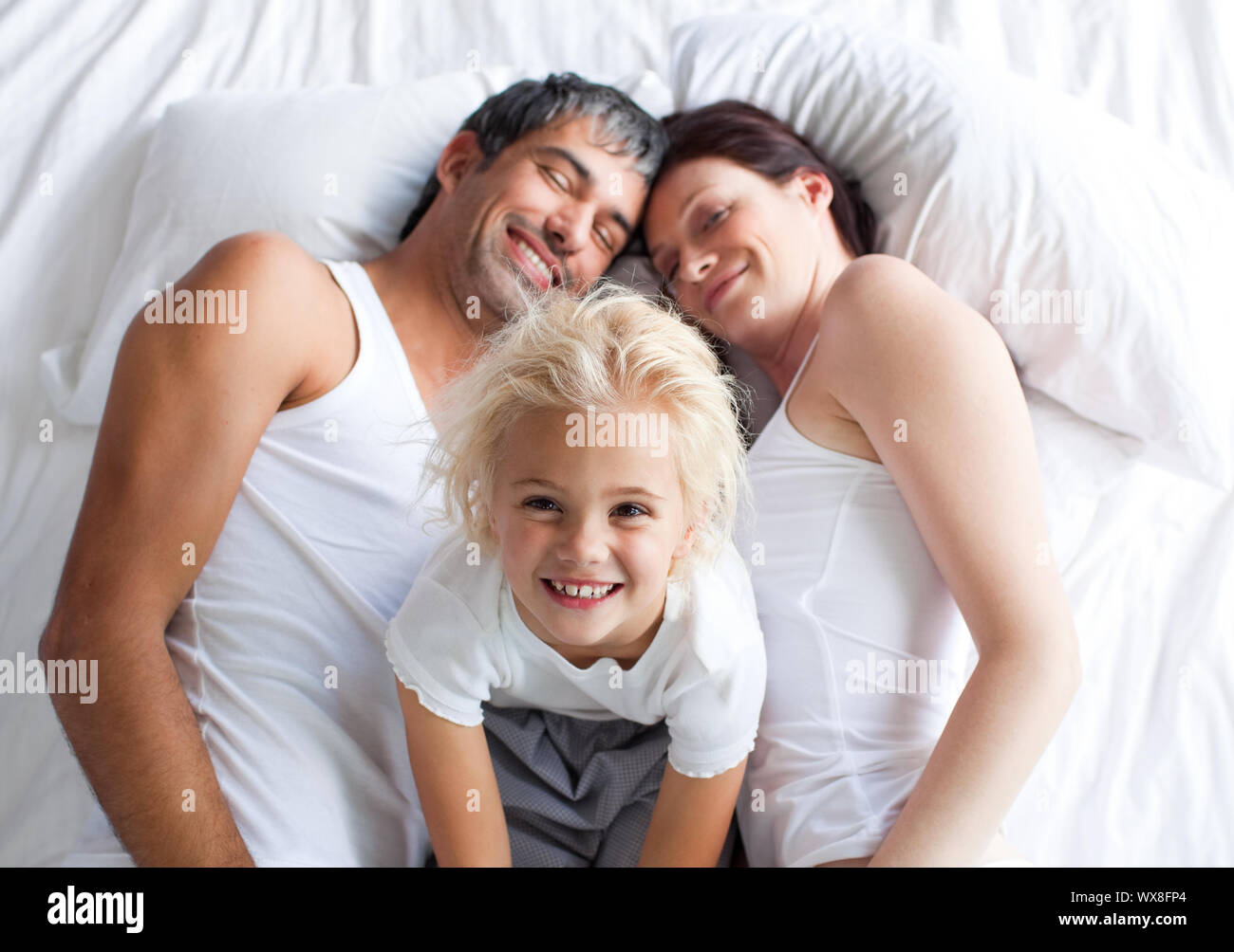 Happy little girl on bed with her parents smiling at the camera Stock ...
