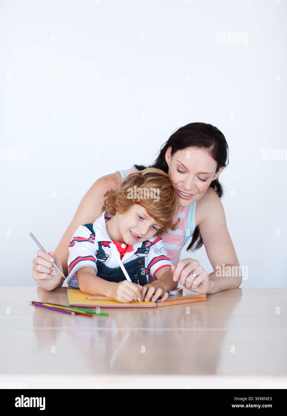 Enamoured mother helping her son drawing against white background Stock ...