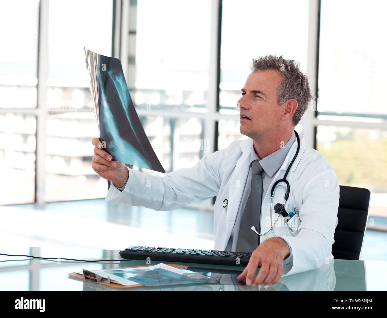 Confident doctor looking on a x-ray sitting at his desk Stock Photo - Alamy