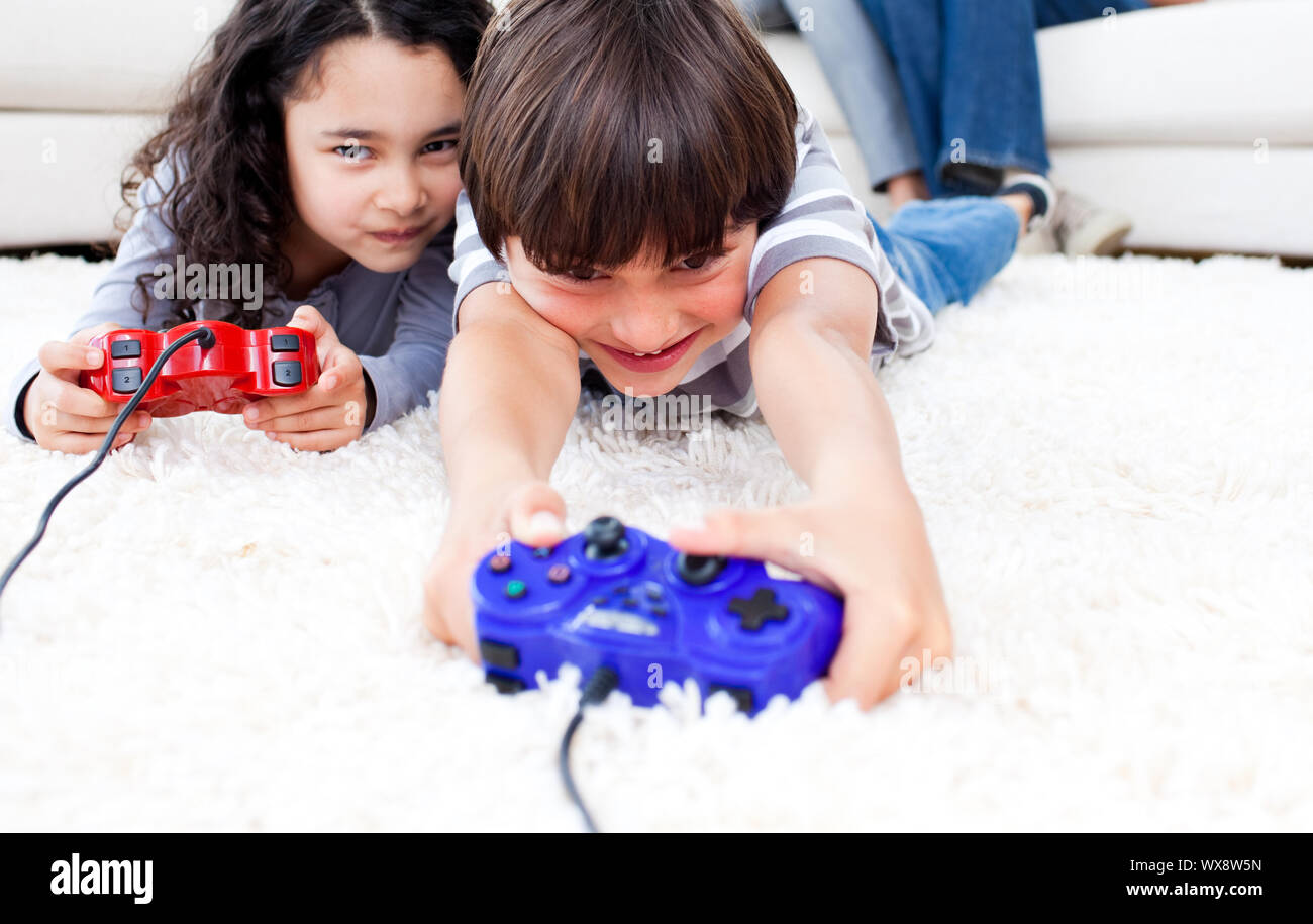 Jolly children playing video games lying on the floor with their ...