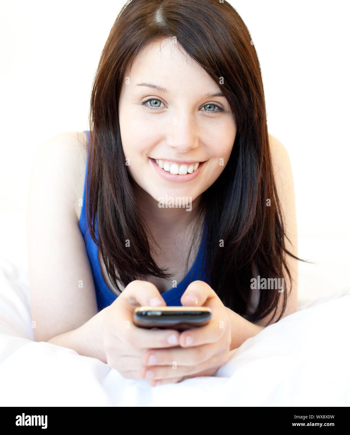 Happy young woman texting while lying on a bed against white background ...