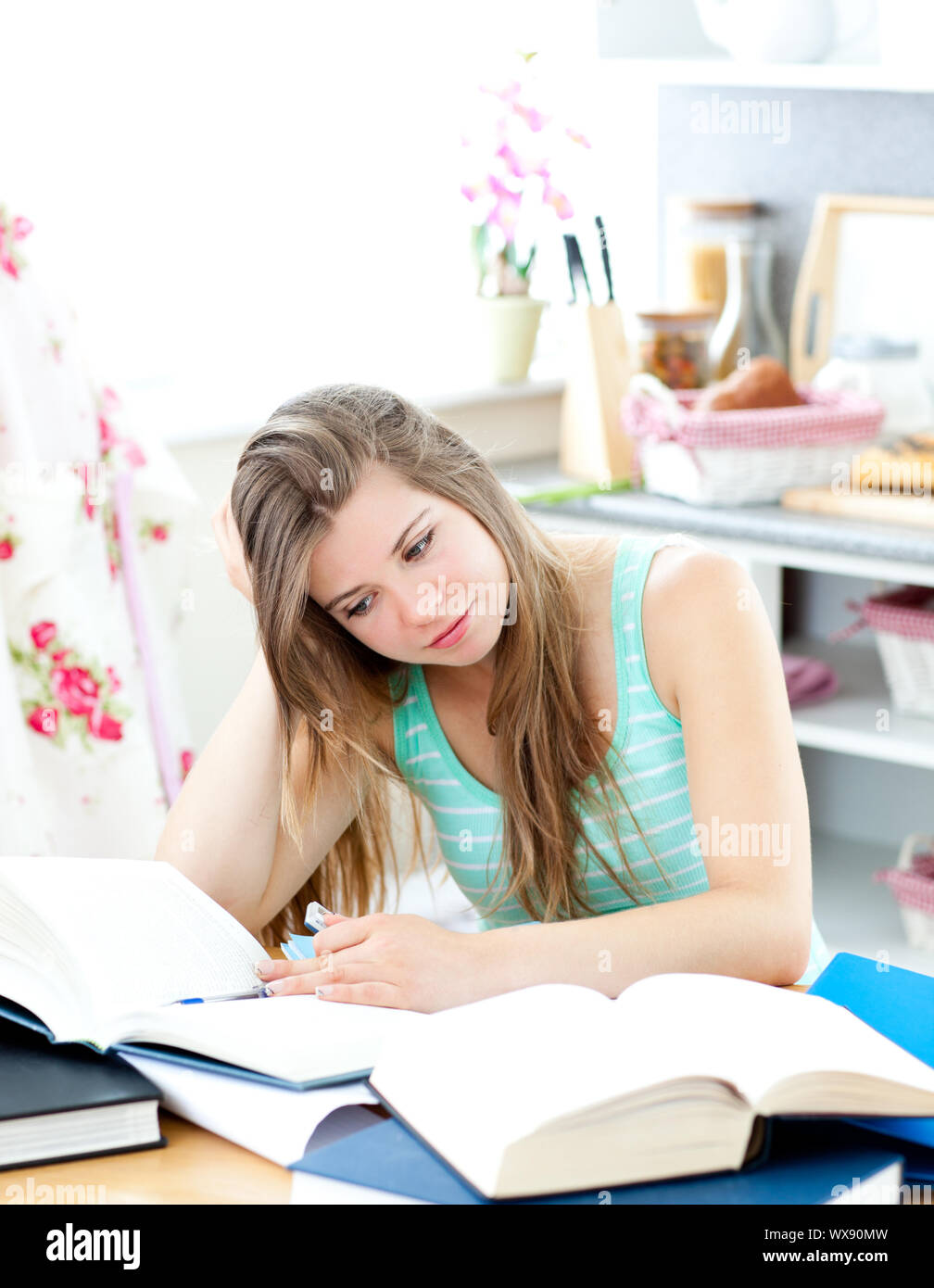 Bored caucasian student doing homework sitting in the kitchen at home ...