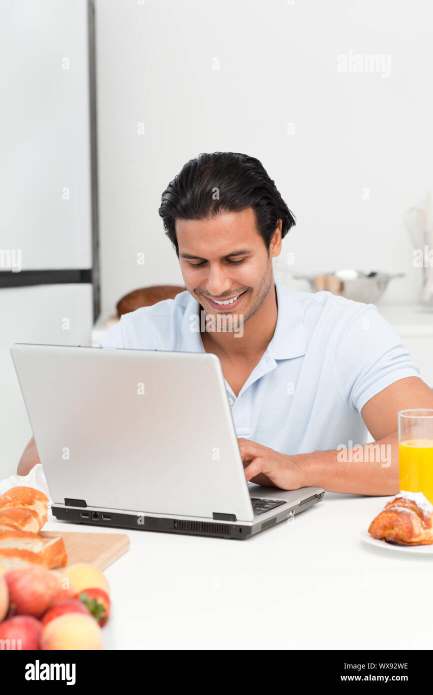 Cheerful man working on his laptop during snack time in his kitchen ...
