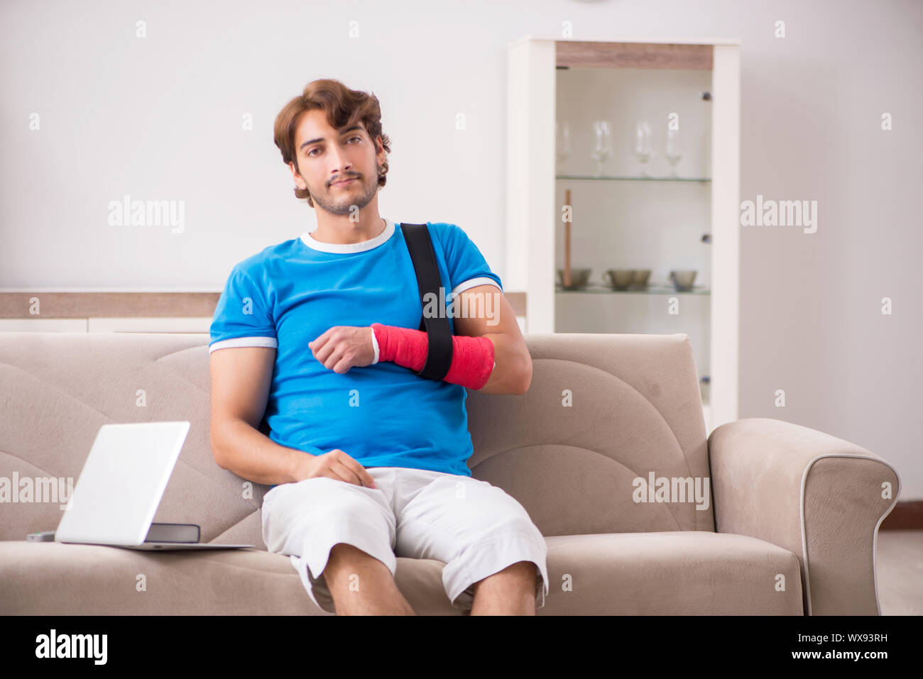 Young man with injured arm sitting on the sofa Stock Photo - Alamy