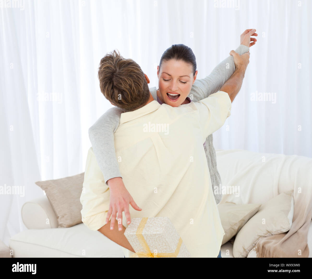 Excited woman catching a present hidden behind her boyfriend in the ...