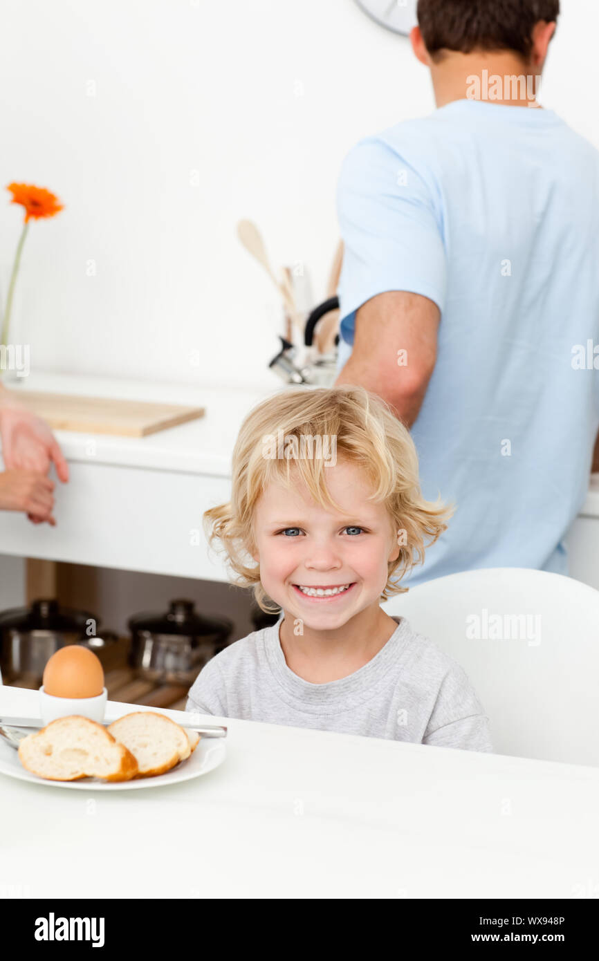 Happy boy eating boiled egg and bread in the kitchen with his father ...