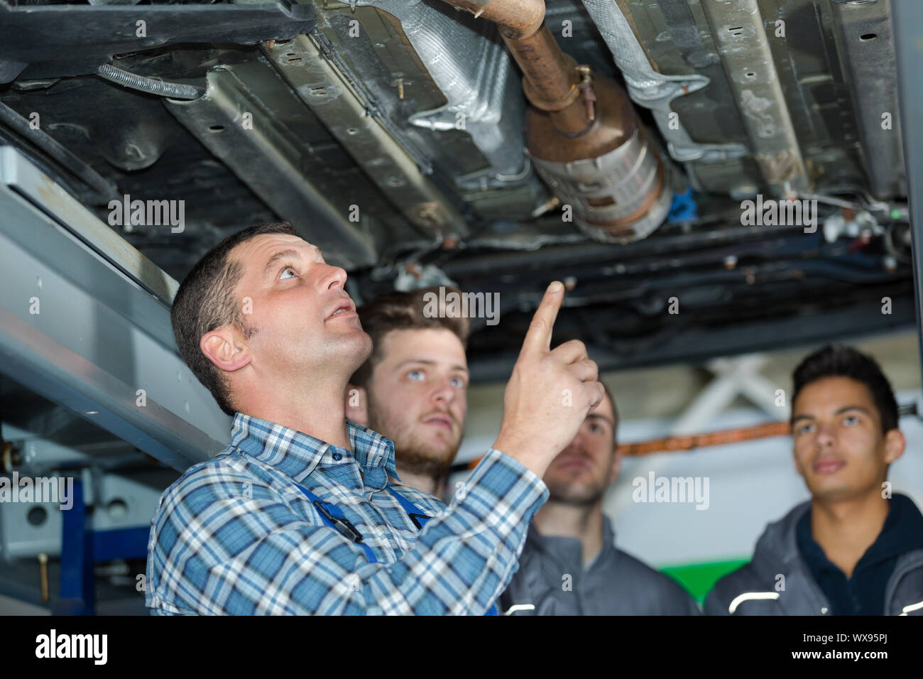 student mechanics looking at underneath of car Stock Photo - Alamy