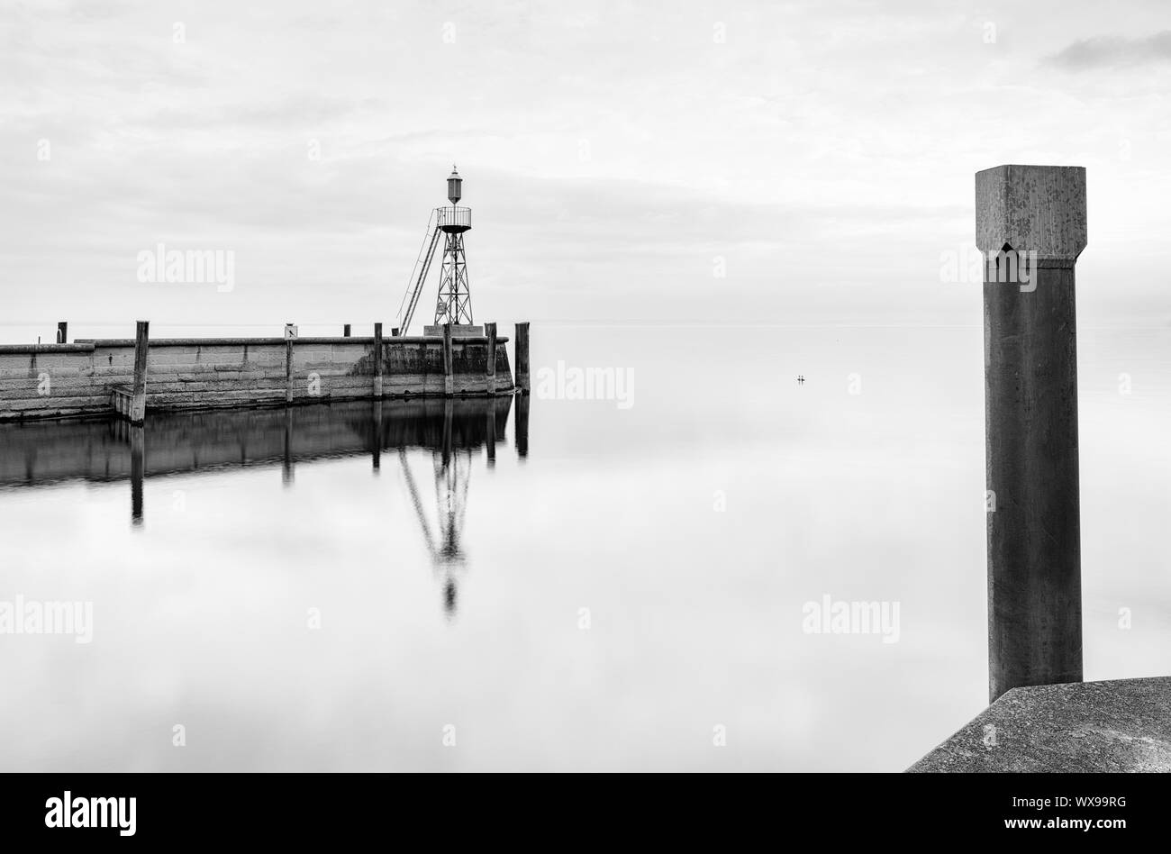 signal light and harbor wall on calm lake waters under an overcast sky ...