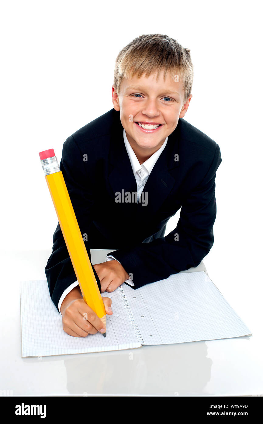 Charming school boy writing his assignment while smiling at camera ...