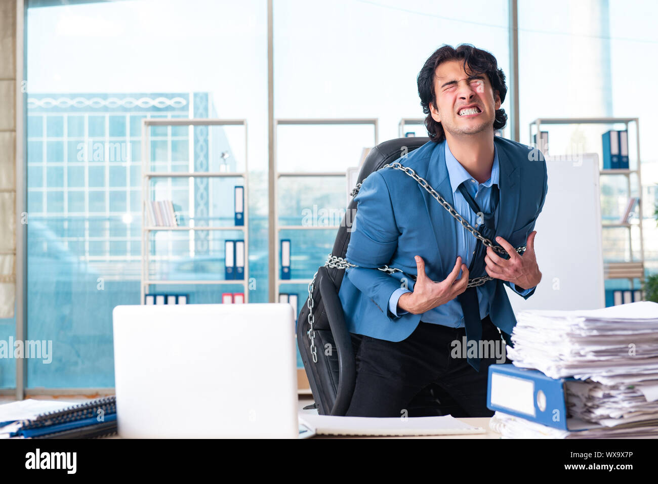 Chained male employee unhappy with excessive work Stock Photo - Alamy