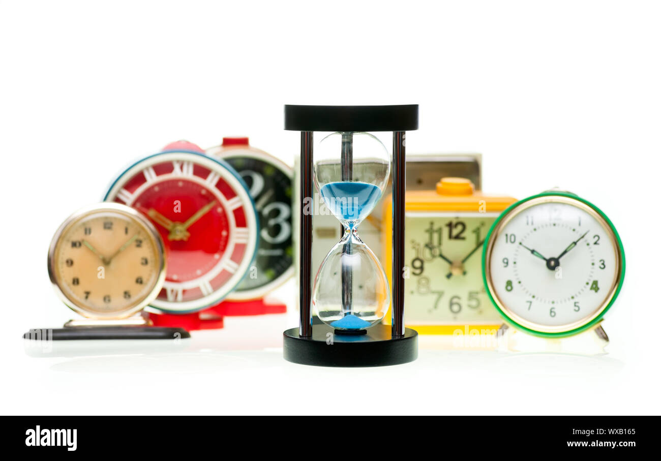 Sand timer with vintage mechanical wind-up alarm clocks on white ...