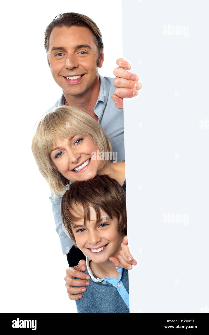 Smiling trio of a father, mother and son peeking from behind an ad ...