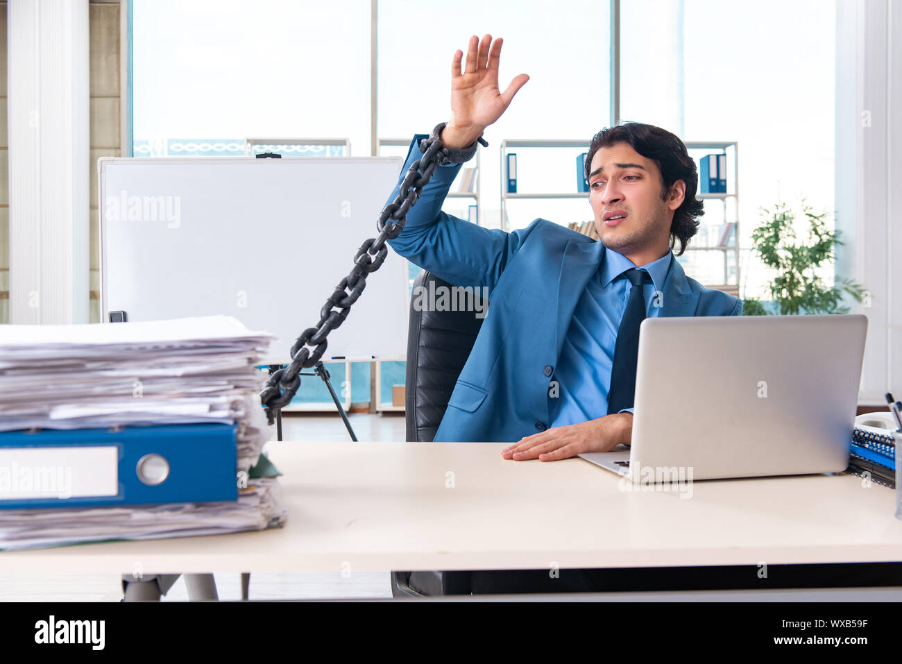 Chained male employee unhappy with excessive work Stock Photo - Alamy