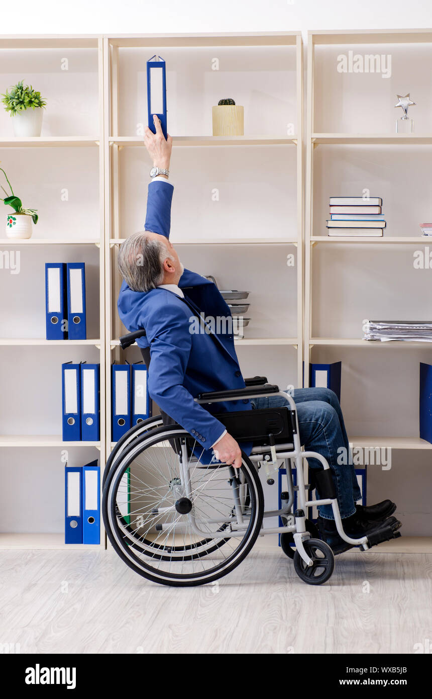 Aged employee in wheelchair working in the office Stock Photo - Alamy