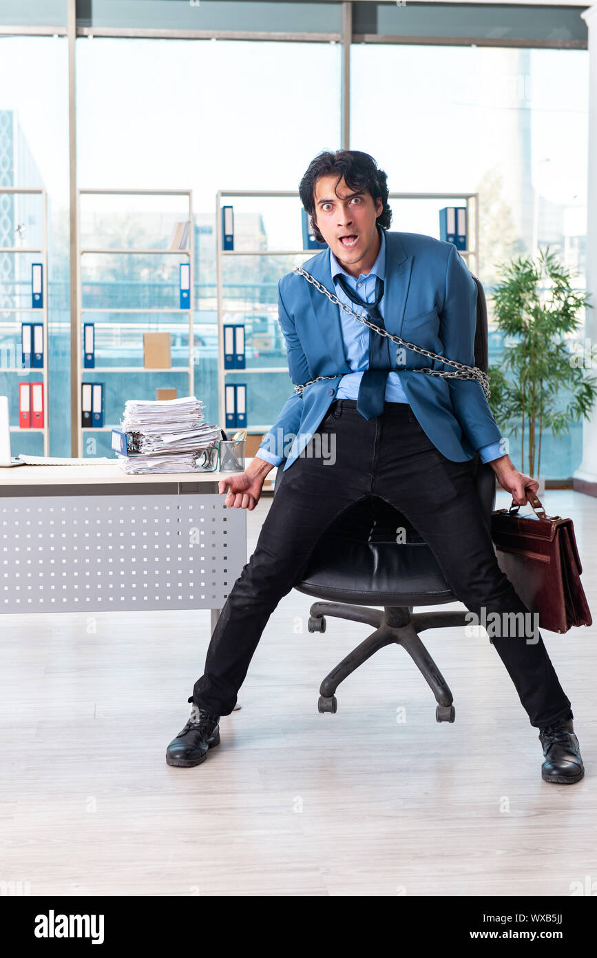Chained male employee unhappy with excessive work Stock Photo - Alamy