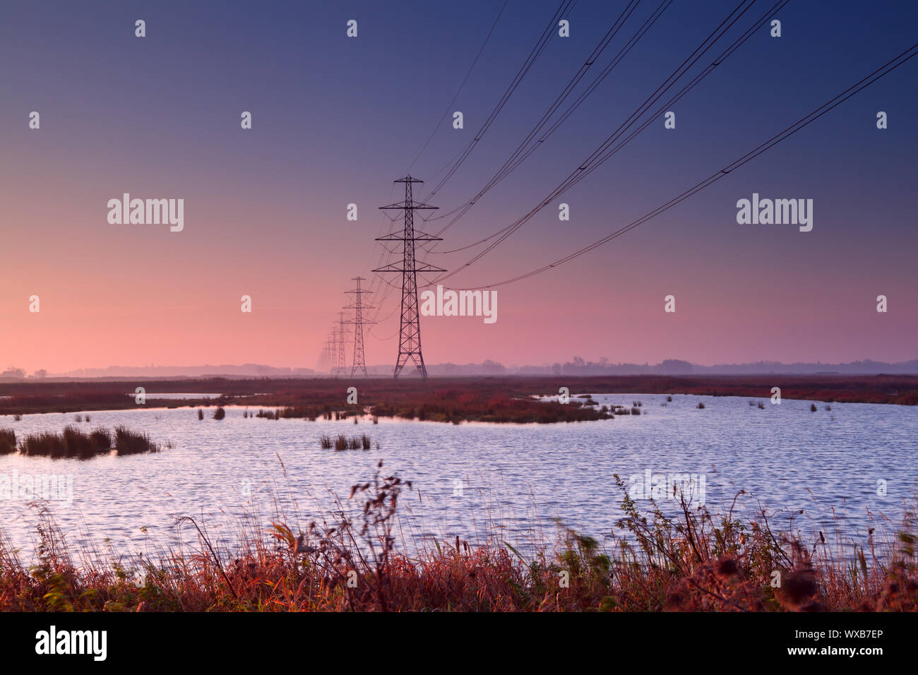 high-voltage electricity line over lakes at early colorful sunrise ...