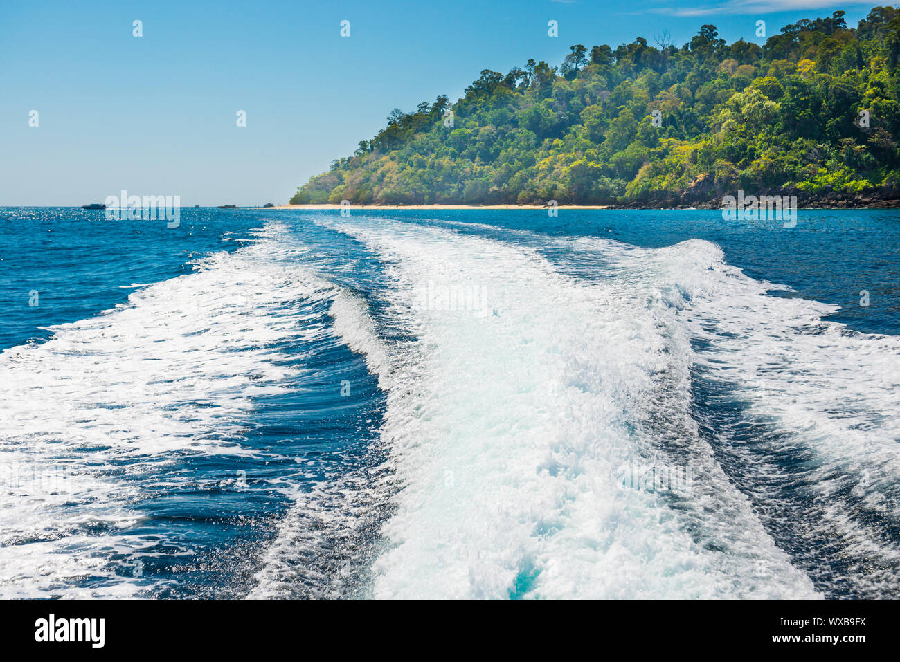 Wake of boat on water surface beside island coast Stock Photo - Alamy
