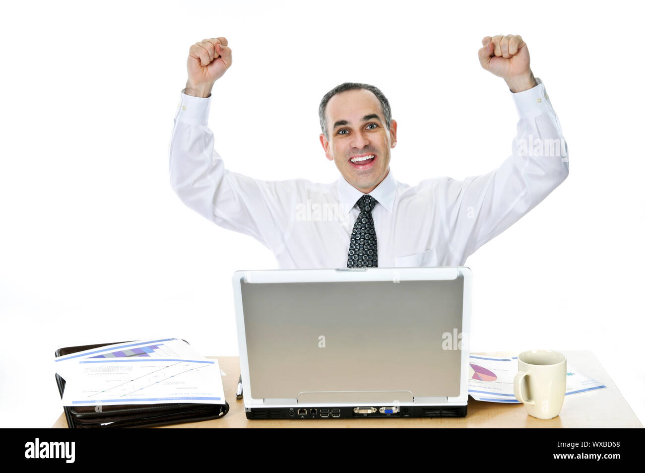 Happy businessman raising his arms sitting at his desk isolated on ...