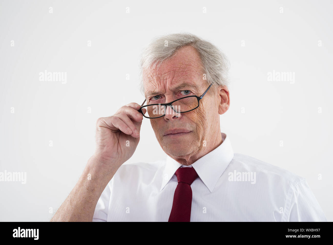 Handsome retired man in glasses peering over the top of the frames at ...