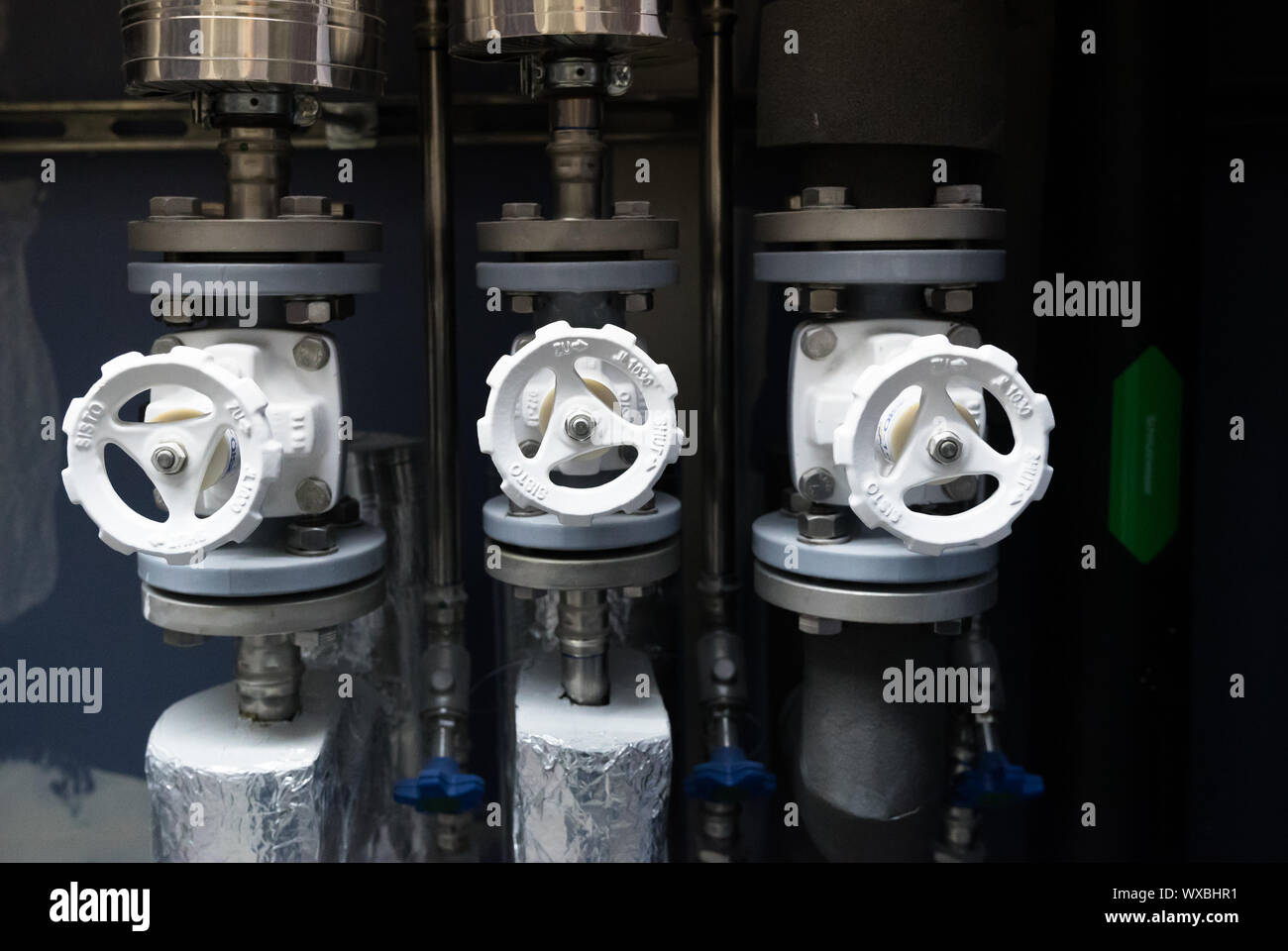 several bright white water mains valves with black and insulated pipes ...