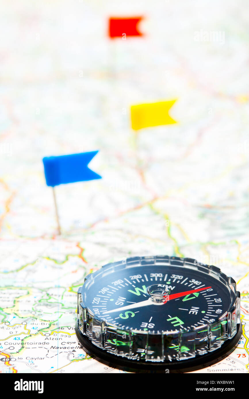 Compass on a map with color flag pins in background Stock Photo - Alamy