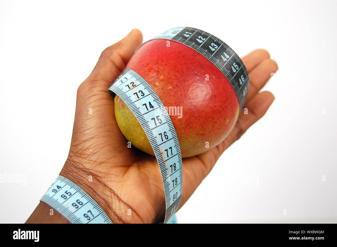 This is an image of a hand holding a mango tied with a measuring tape ...