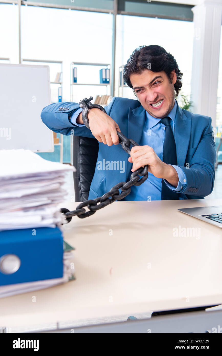 Chained male employee unhappy with excessive work Stock Photo - Alamy