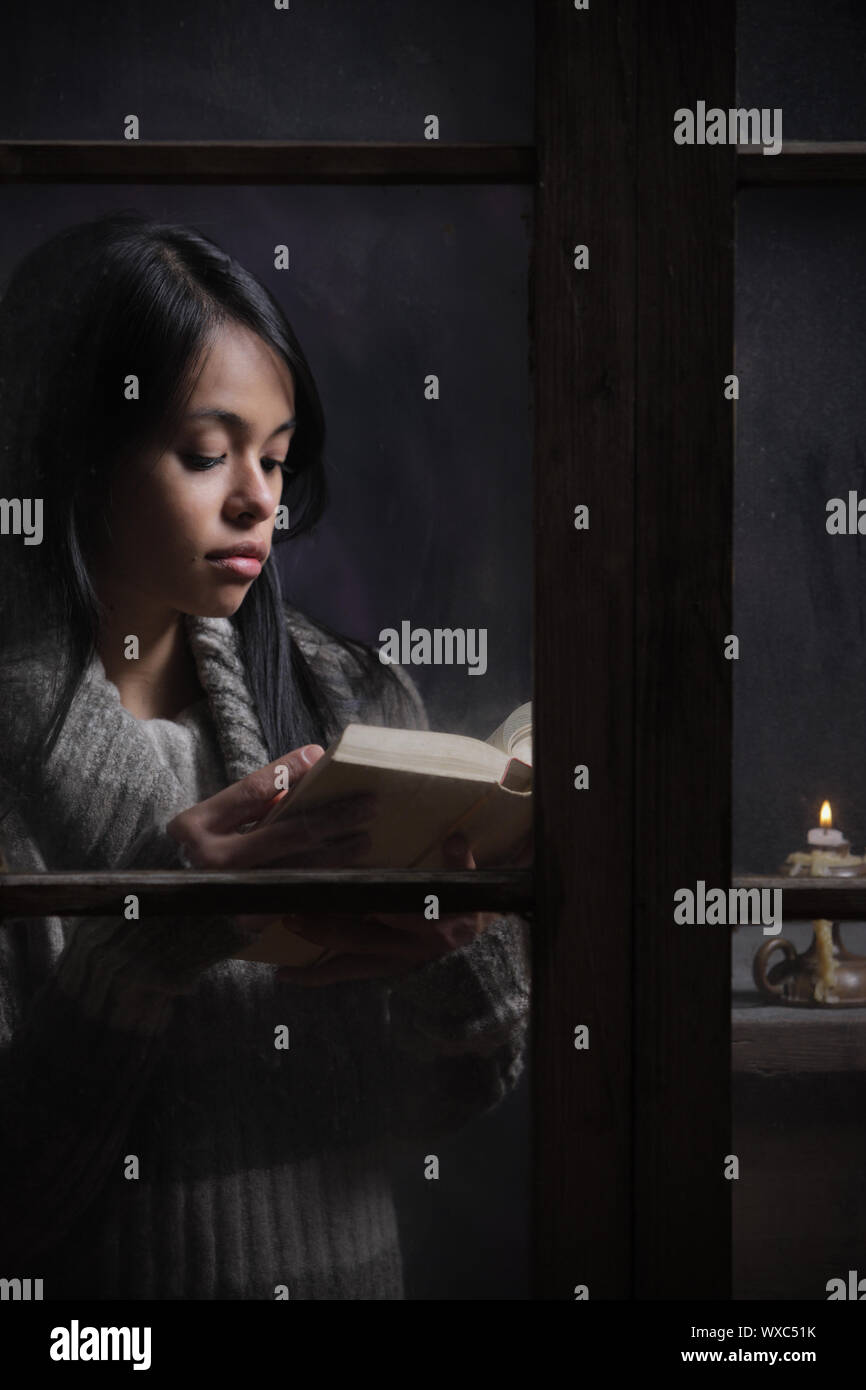 Portrait of a beautiful woman behind window reading a book Stock Photo ...