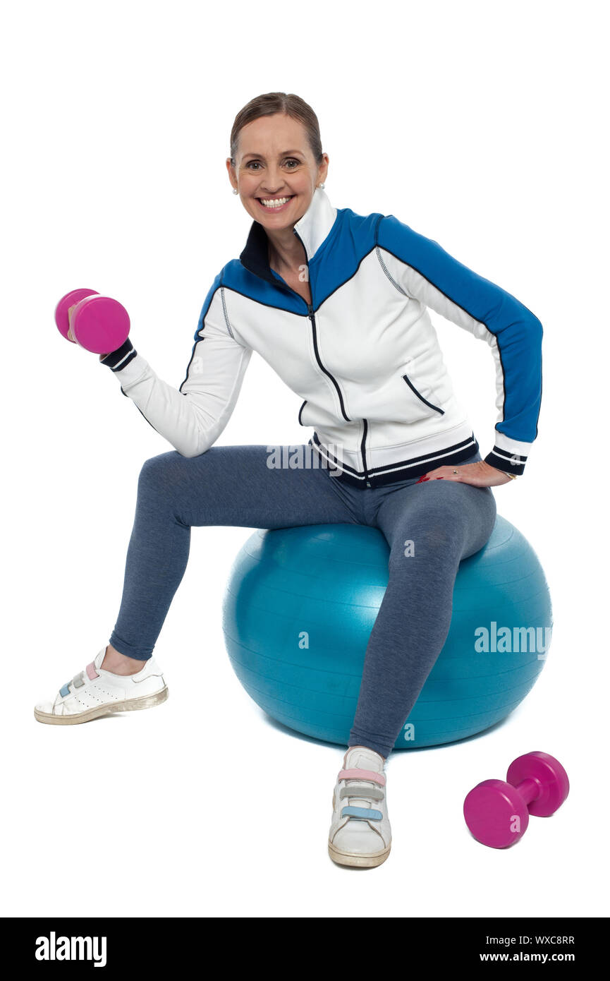 Fit woman doing biceps exercise with pink dumbbells. Sitting on big ...