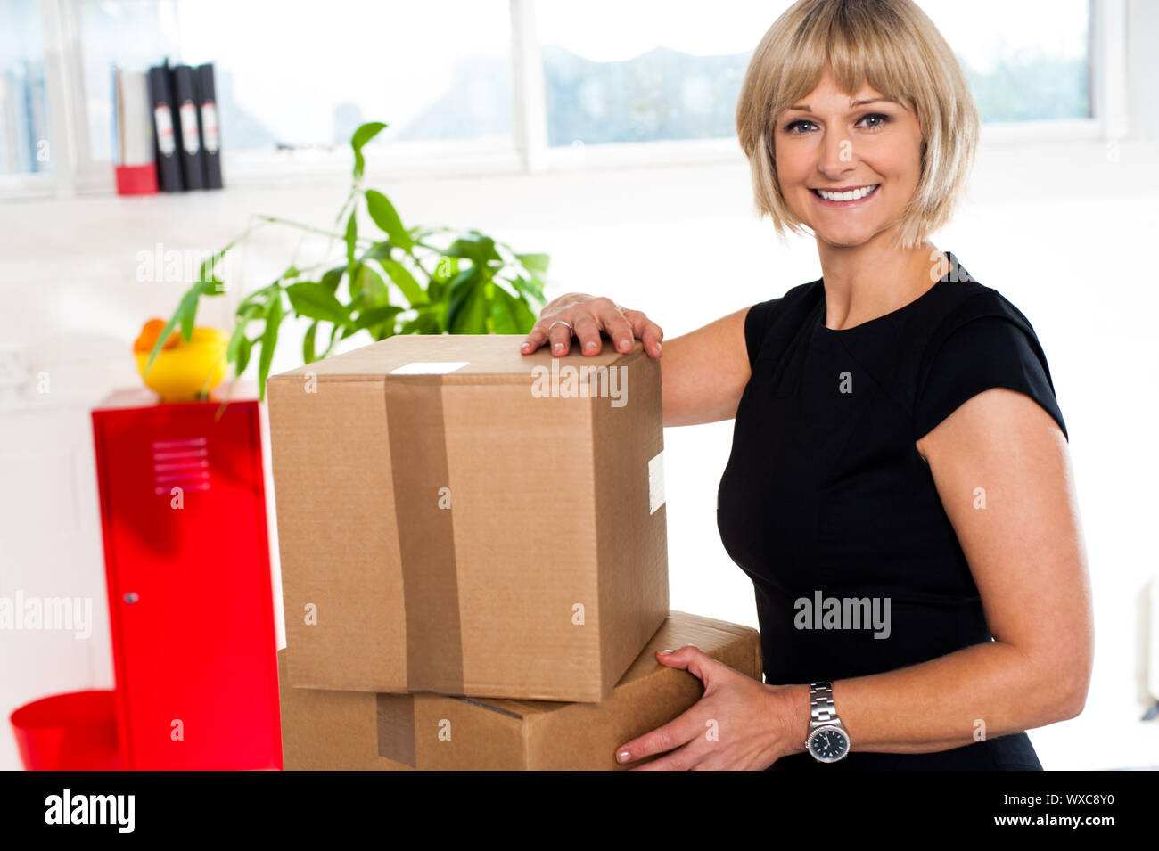 Helper woman in office posing beside cardboard cartons ready to be ...