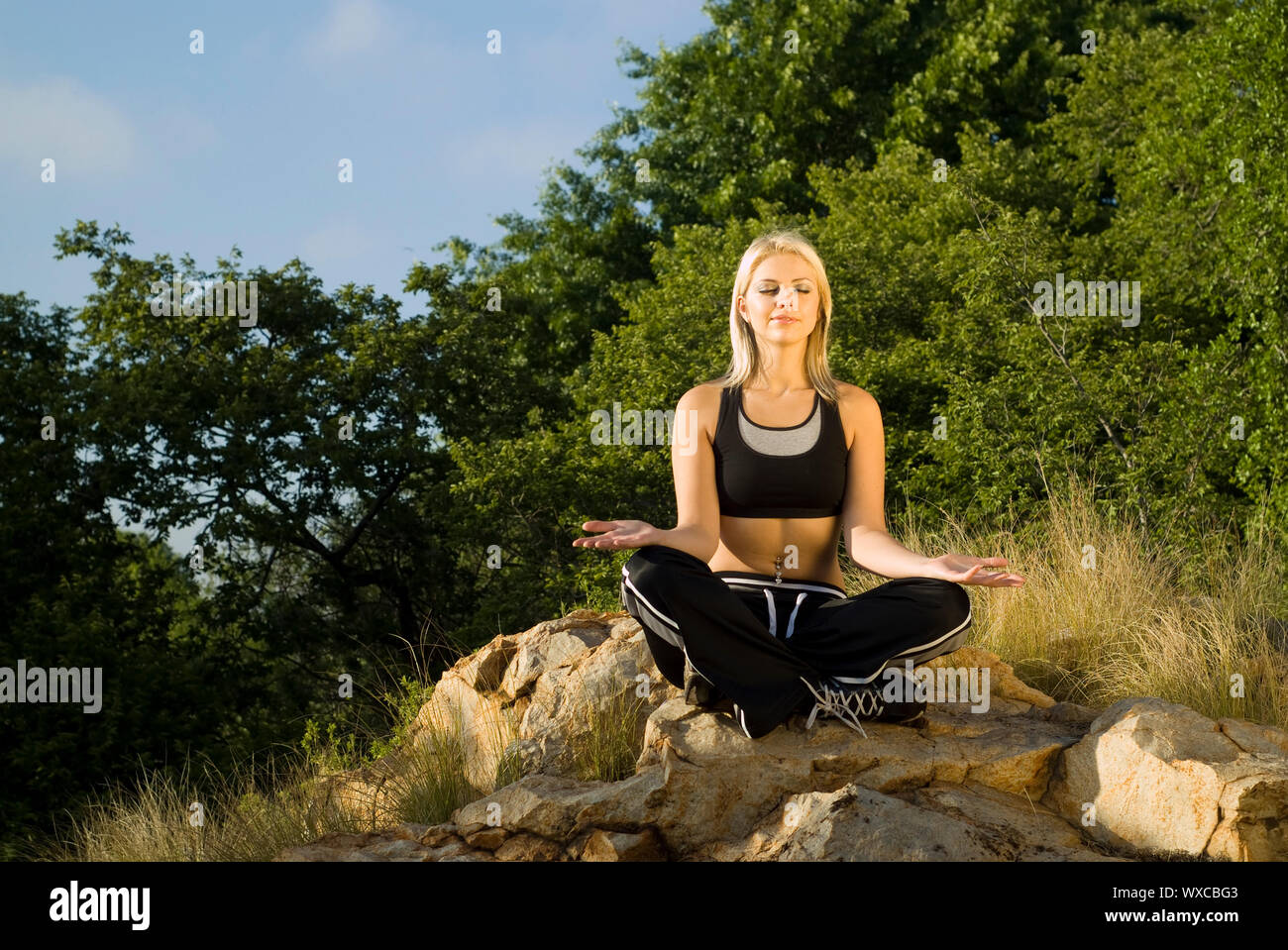 Pretty woman meditating on rock eyes closed with gold light reflector ...