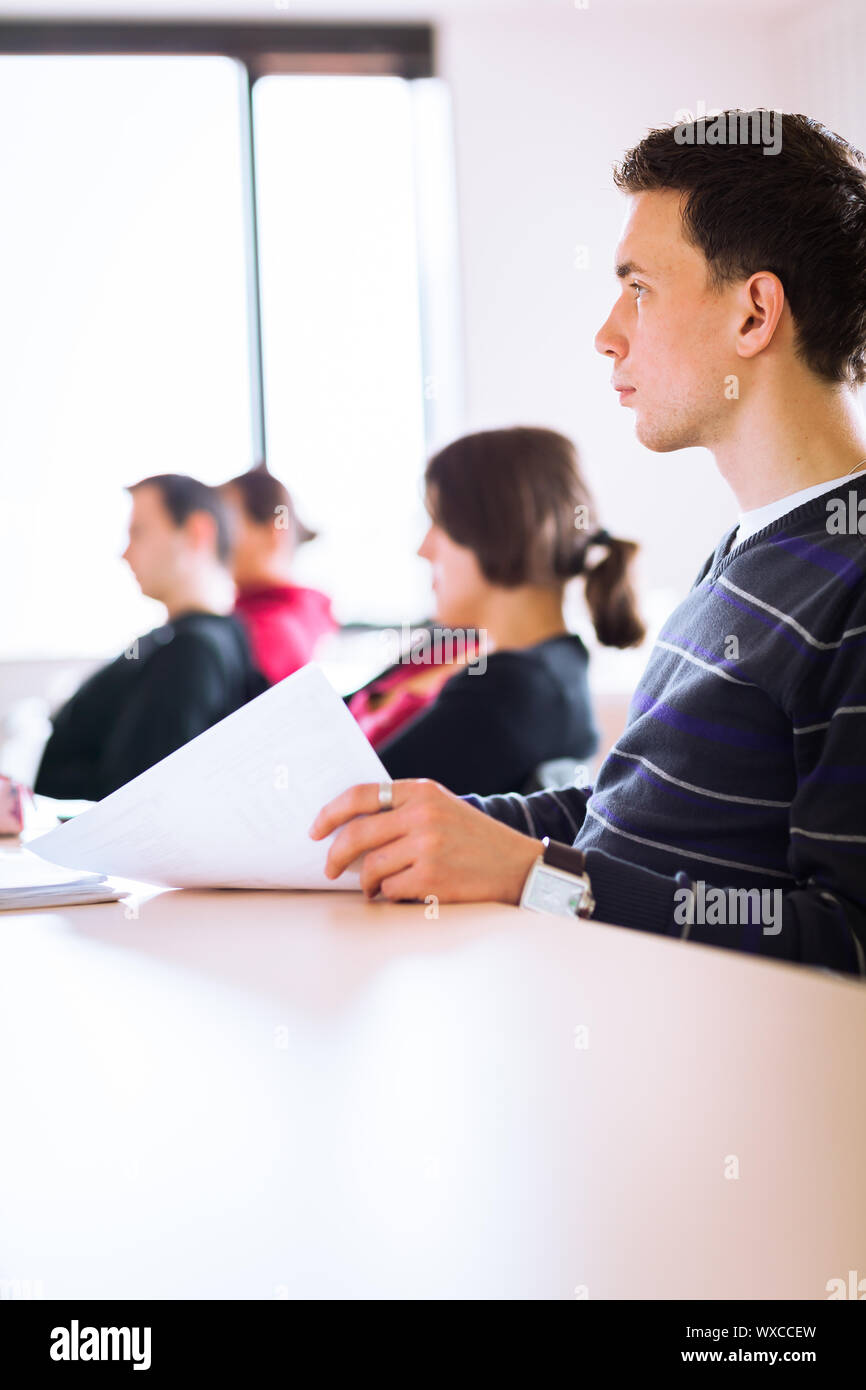 young, handsome male college student sitting in a classroom full of ...
